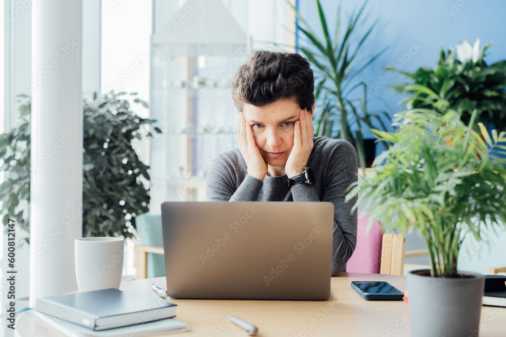 Middle aged shocked business woman sitting in front of laptop looking ...