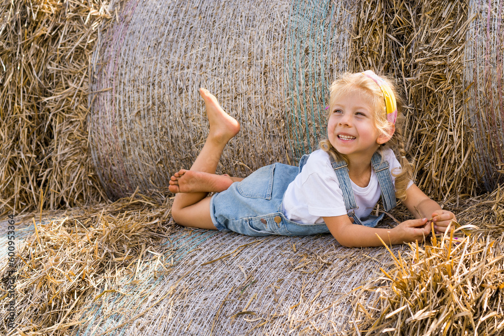 Little blonde girl lying on a pile of hay, happy childhood in the ...