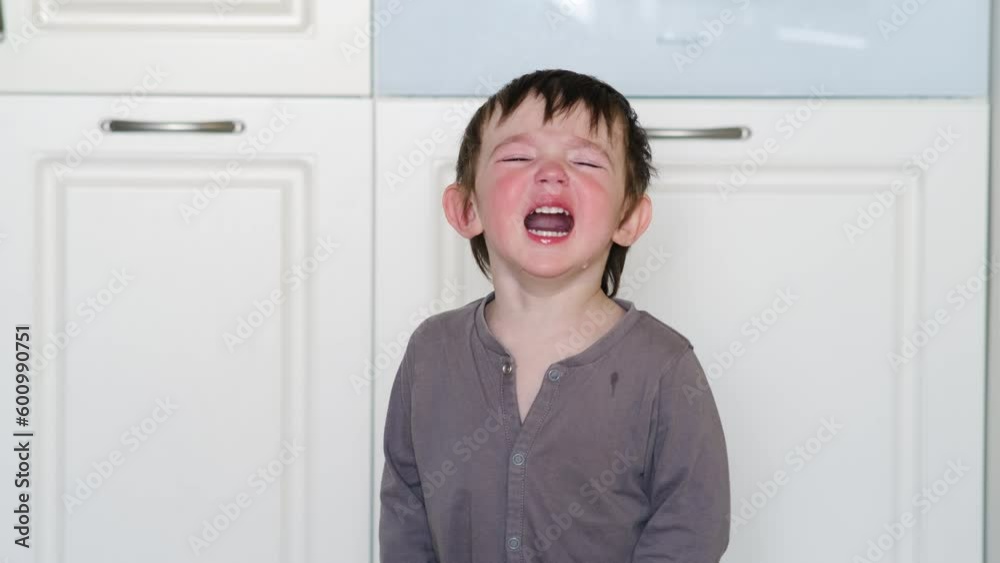 Portrait of a crying toddler baby in gray clothes on the background of ...