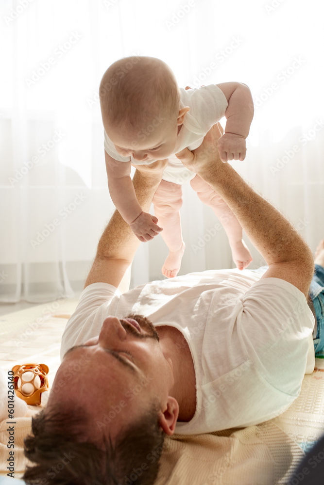 Happy dad holds his newborn baby in his arms while lying on the floor ...
