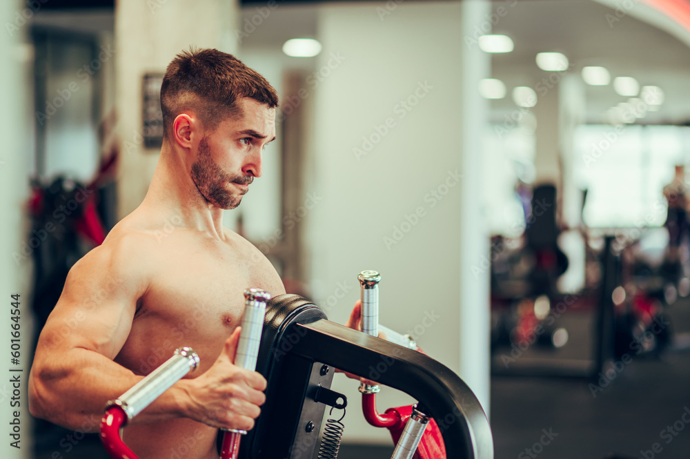 Foto de A shirtless muscular man is sitting at the chest pull machine ...