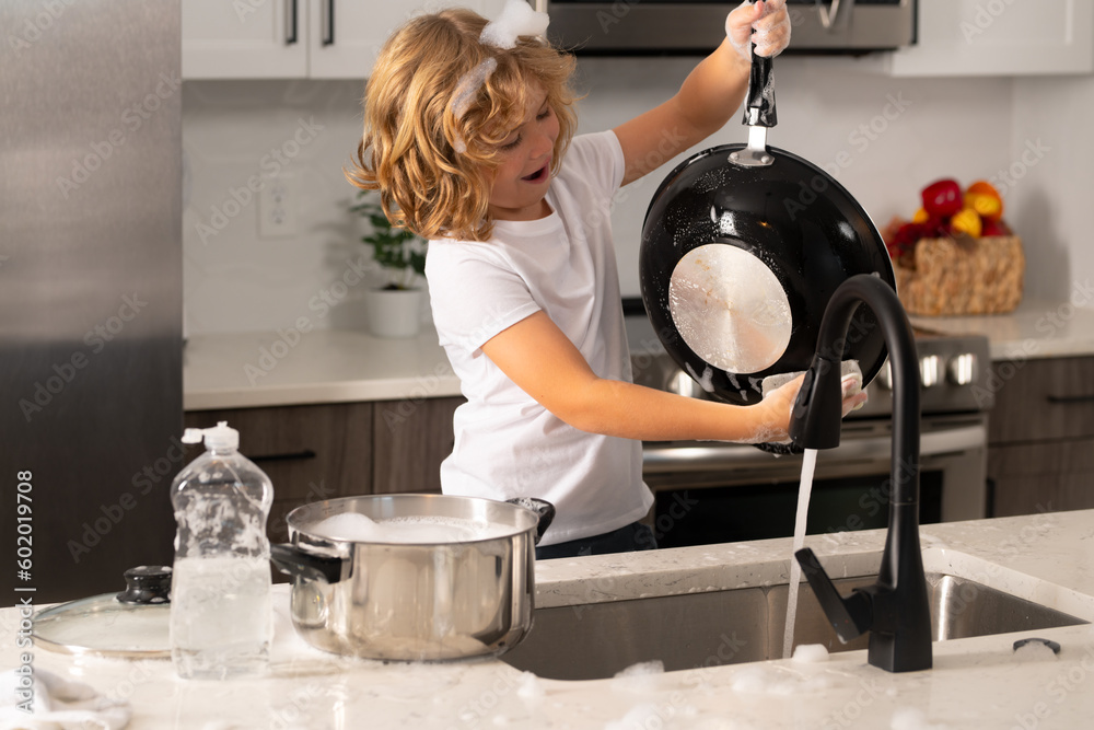 Kid washing dishes in the kitchen interior. Child helping his parents ...