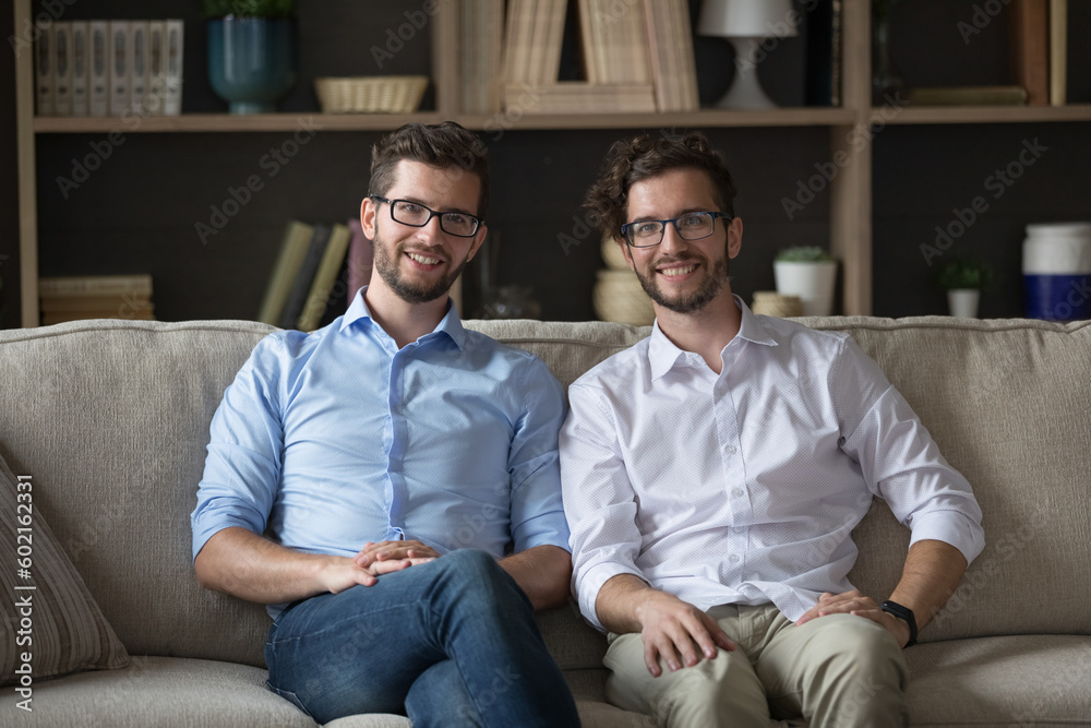 Happy positive young adult identical twin men in glasses sitting ...
