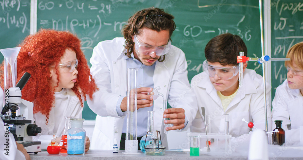 Concentrated pupils with male young teacher doing chemical experiment ...