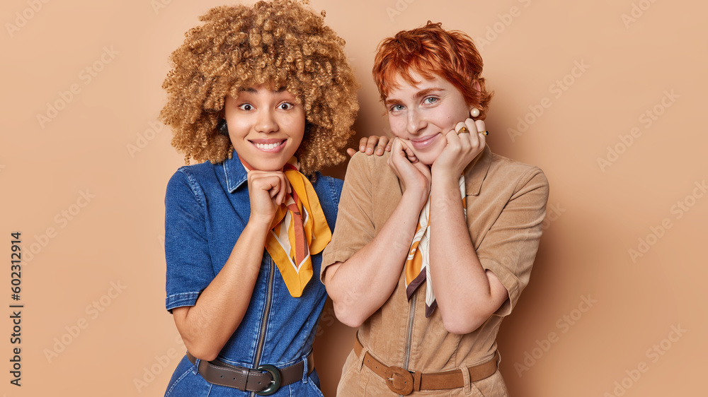 Horizontal shot of two pretty young women keep hands under chin stand ...
