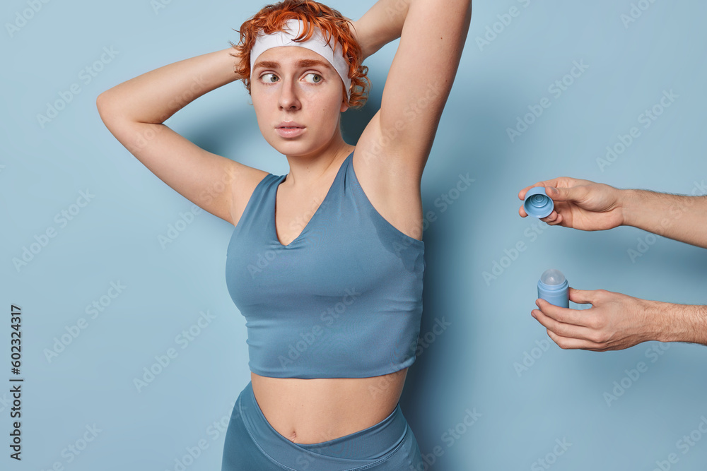 Embarrassed ginger sporty woman keeps arms raised up stands sweaty ...