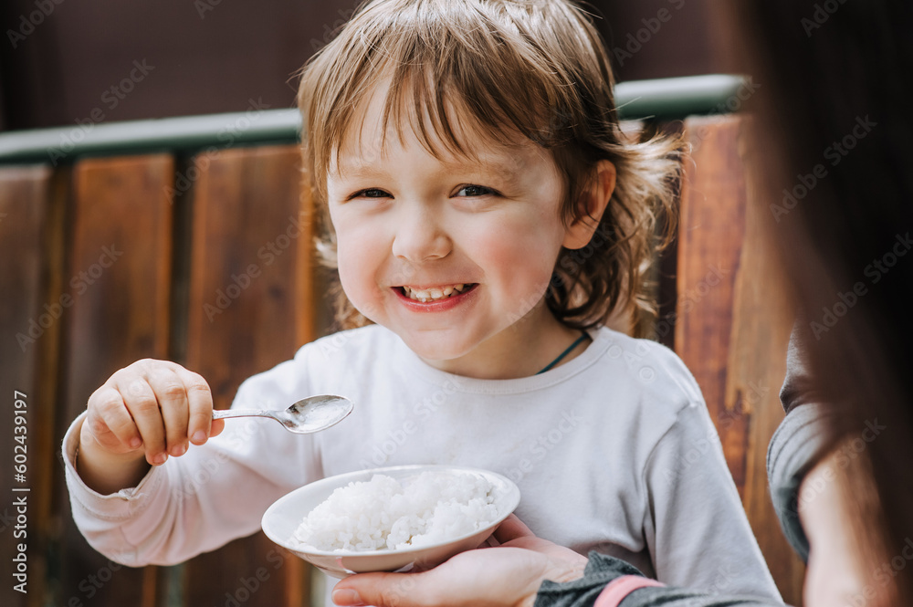 A beautiful little boy, a child eats rice porridge with a spoon in his ...