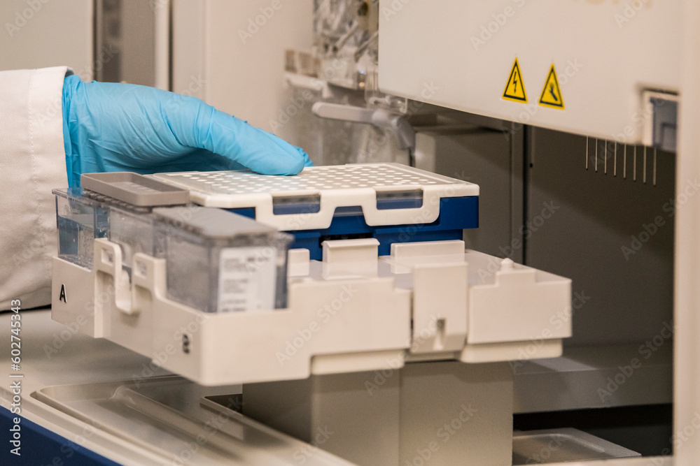 A hand with blue nitril gloves puting a PCR plate into a sanger genetic ...