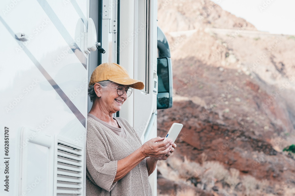 Happy senior woman with eyeglasses standing outside a camper van motor ...