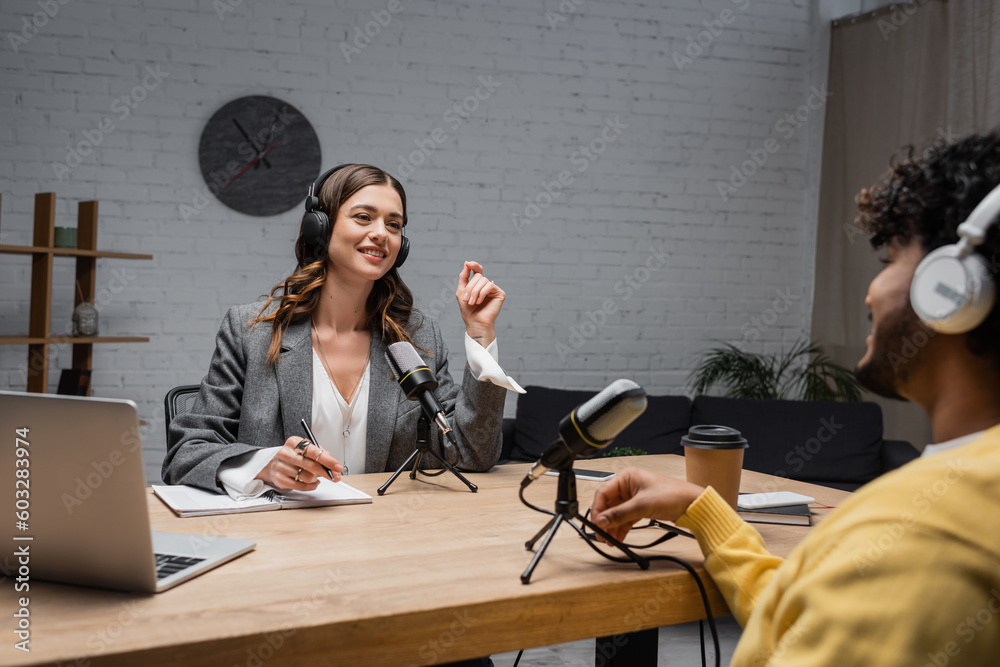 Foto de positive female podcast host in wireless headphones talking to ...