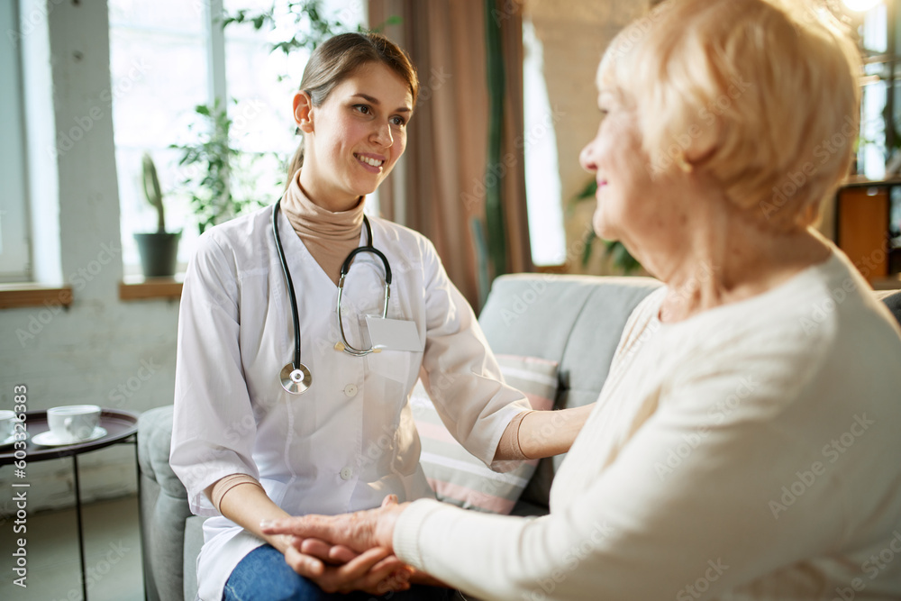 Smiling young woman, doctor giving support and hope to her elderly ...