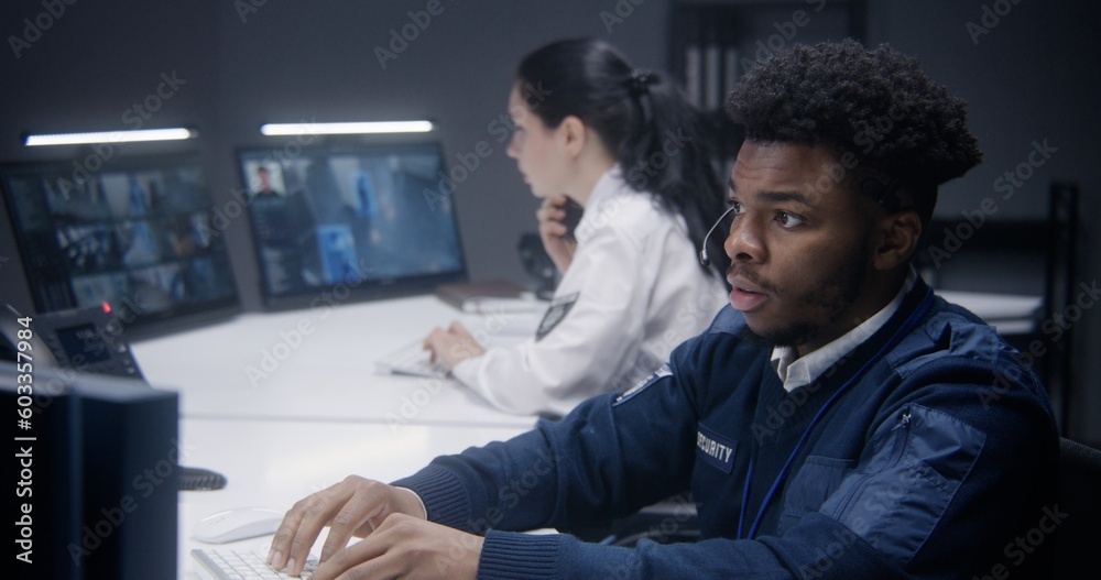 African American security operator in headset types keyboard and looks ...