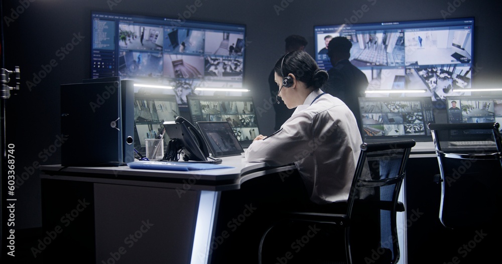 Female security officer in headset zooms and controls CCTV cameras ...
