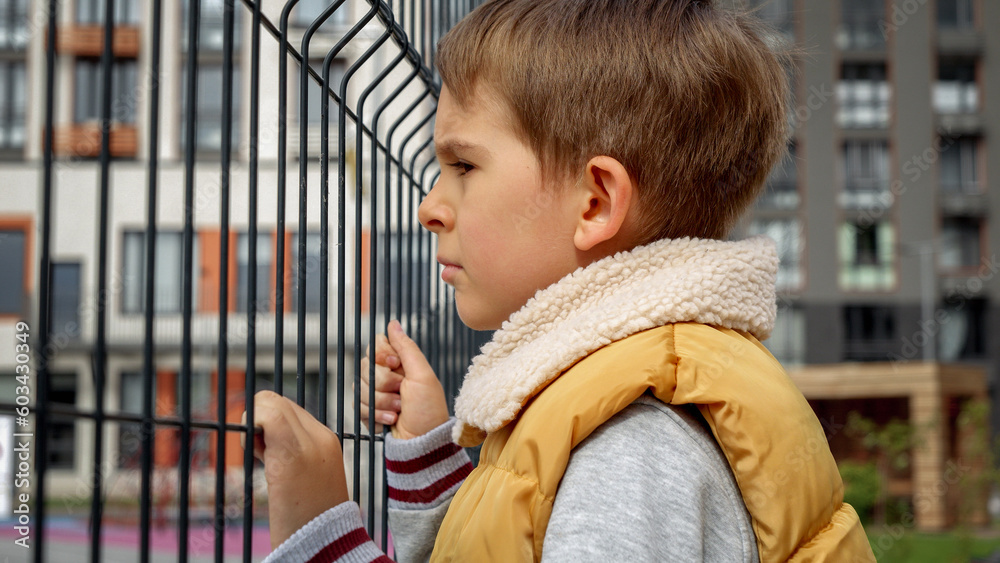 Portrait of sad little boy looking through metal fence. Child ...