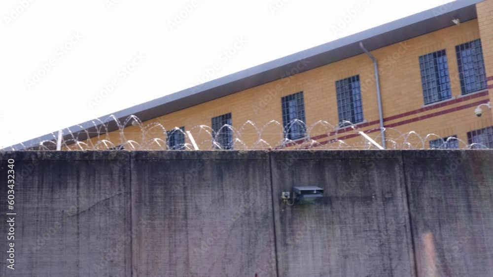 high concrete fence, barbed wire fence on top, pre-trial detention cell ...