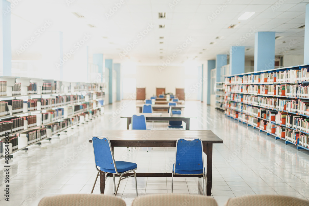 An empty college library with open spaces, blue chairs and book stacks ...