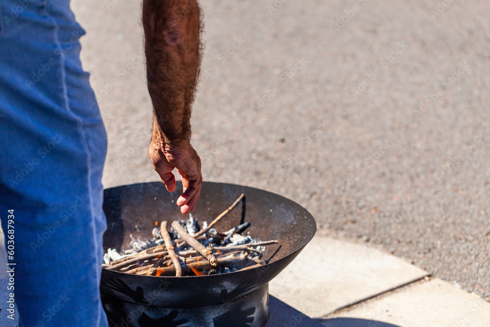 Aboriginal elder putting sticks in fire pit for smoking ceremony during ...