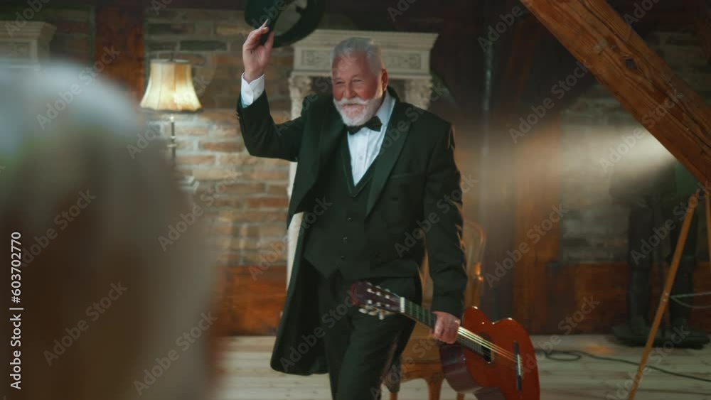 Elderly male musician, actor, or showman goes on stage with a guitar ...