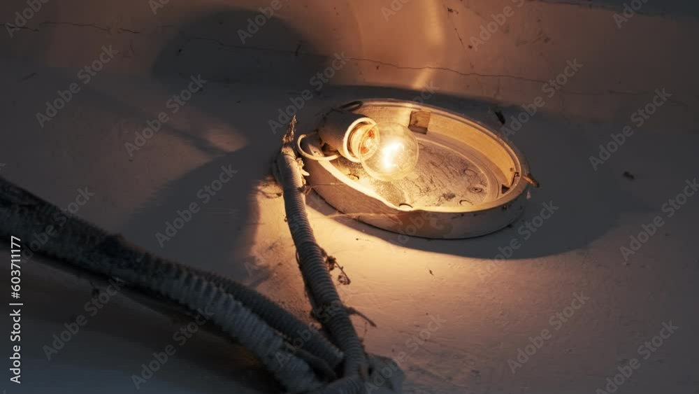 An incandescent light bulb glows in an old broken lamp on the concrete ...