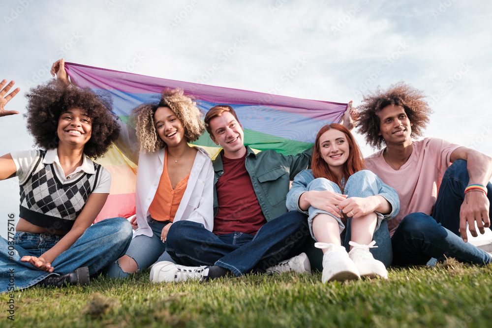 Group of young people sitting on the grass with the gay pride flag ...