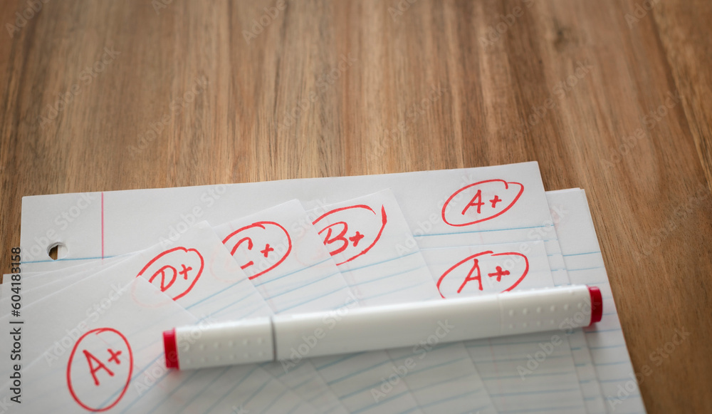 Different grades school paper marked in red ink over a wood desktop ...