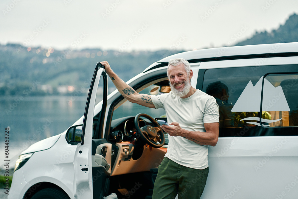 Happy older man standing near rv camper van on vacation using mobile ...