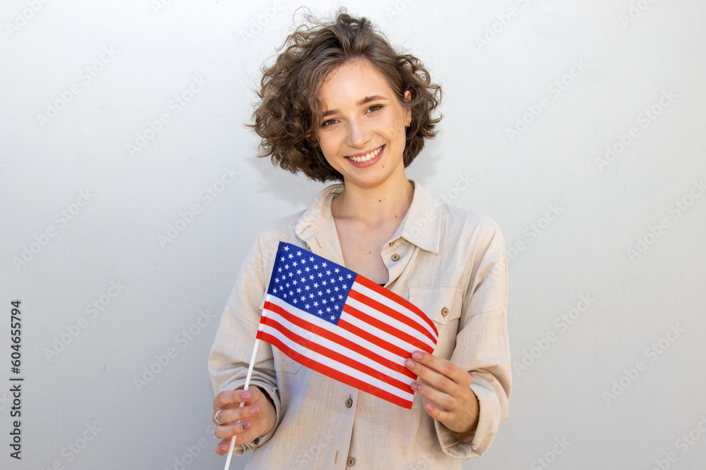 Young smiling happy fun woman hold US flag look camera on gray wall ...