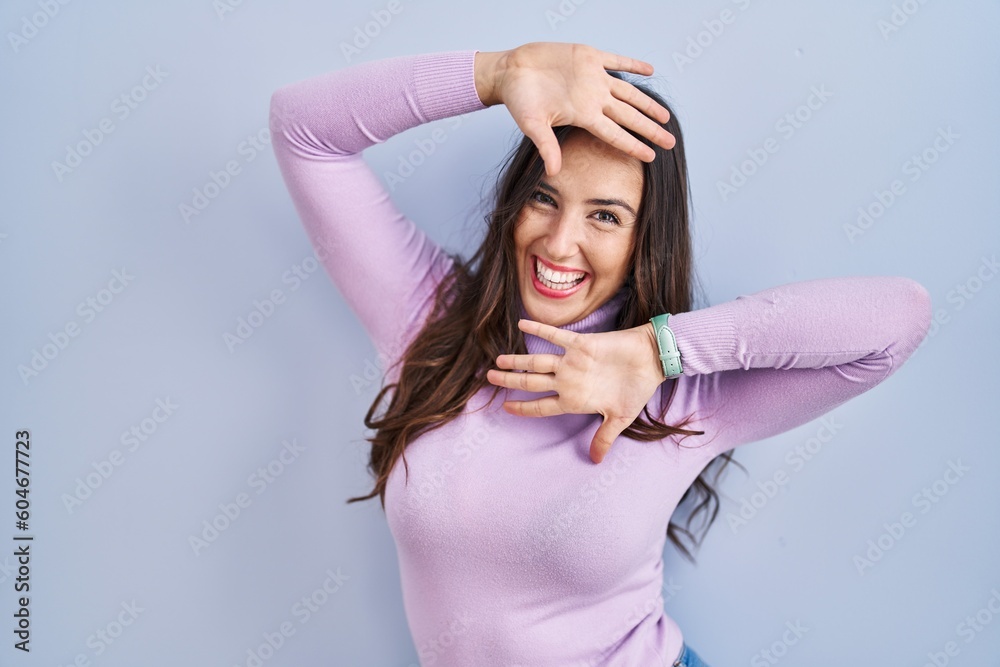 Young brunette woman standing over blue background smiling cheerful ...