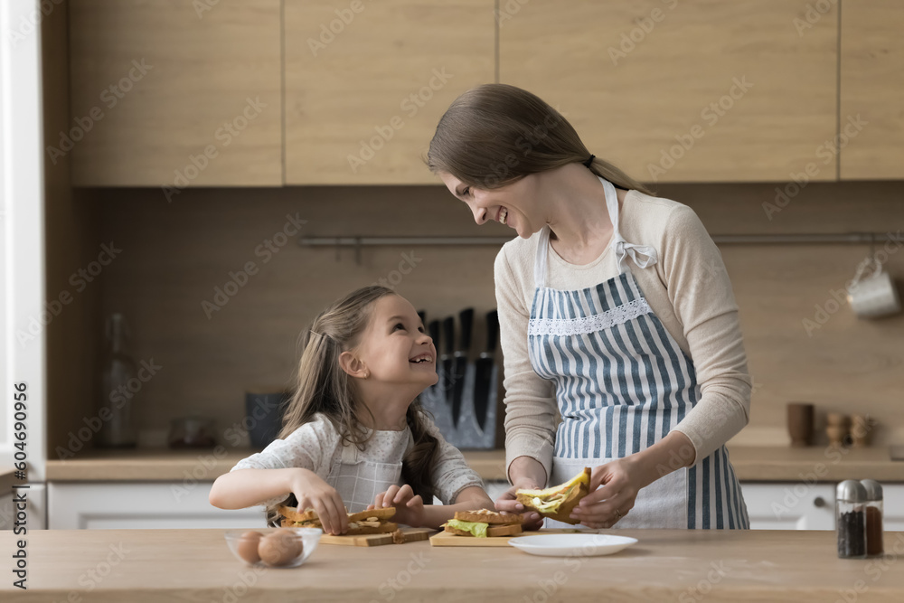 Attractive lovely woman and little daughter in aprons cooking together ...