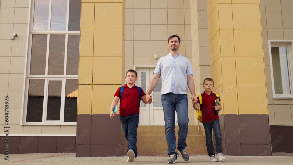 father leads child with backpacks school. two boy sons go school ...