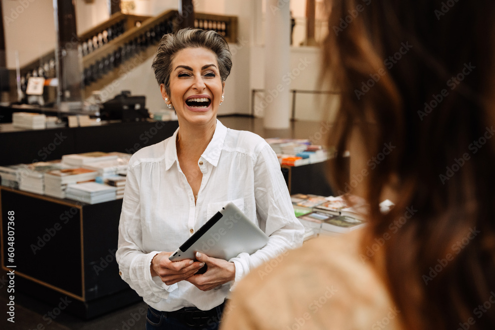 Cheerful mature woman art gallery manager holding tablet and talking to someone while working in ...