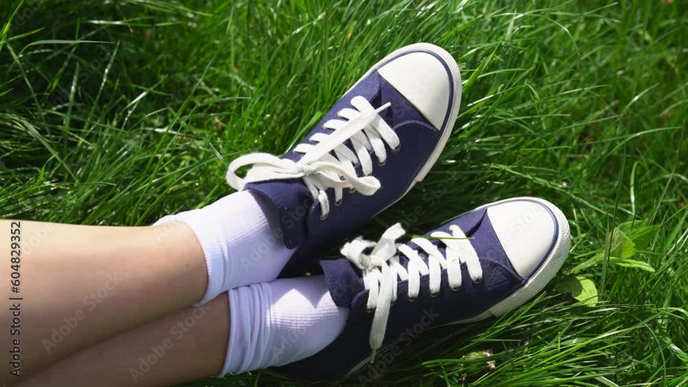 The crossed legs of a teenage girl in white socks and blue sneakers ...