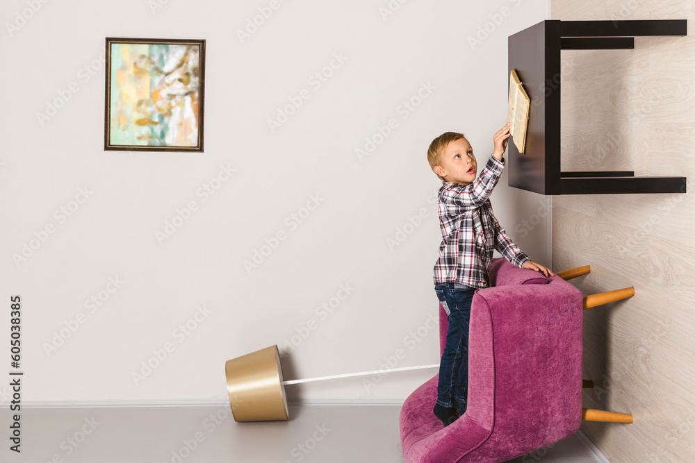 Little boy in the upside down room, reaching his hand to the table and ...