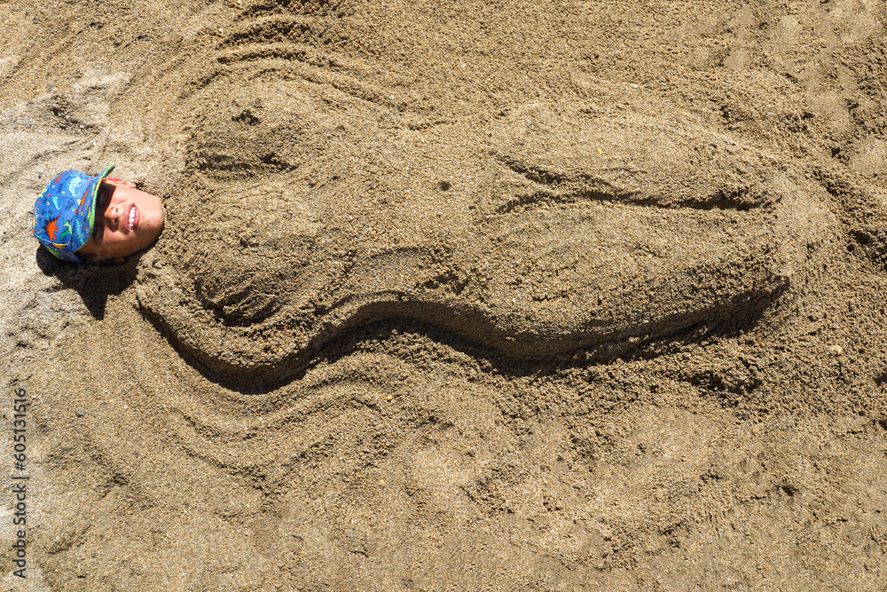 The boy's head peeks out of the sand, the body is buried in the sand ...