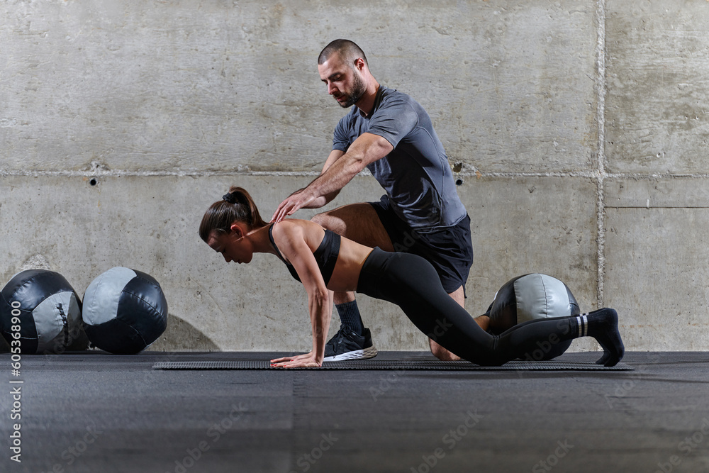 A muscular man assisting a fit woman in a modern gym as they engage in ...