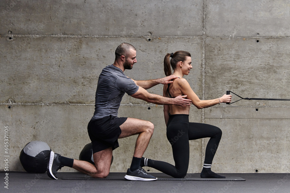 A muscular man assisting a fit woman in a modern gym as they engage in ...