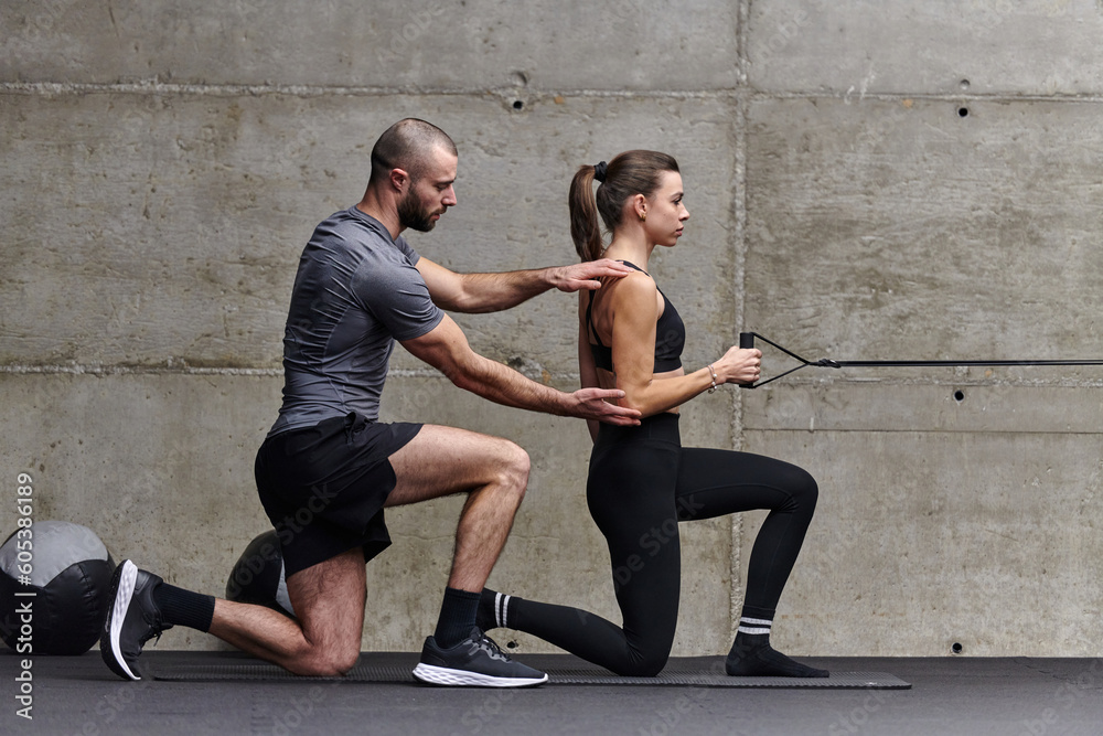 A muscular man assisting a fit woman in a modern gym as they engage in ...