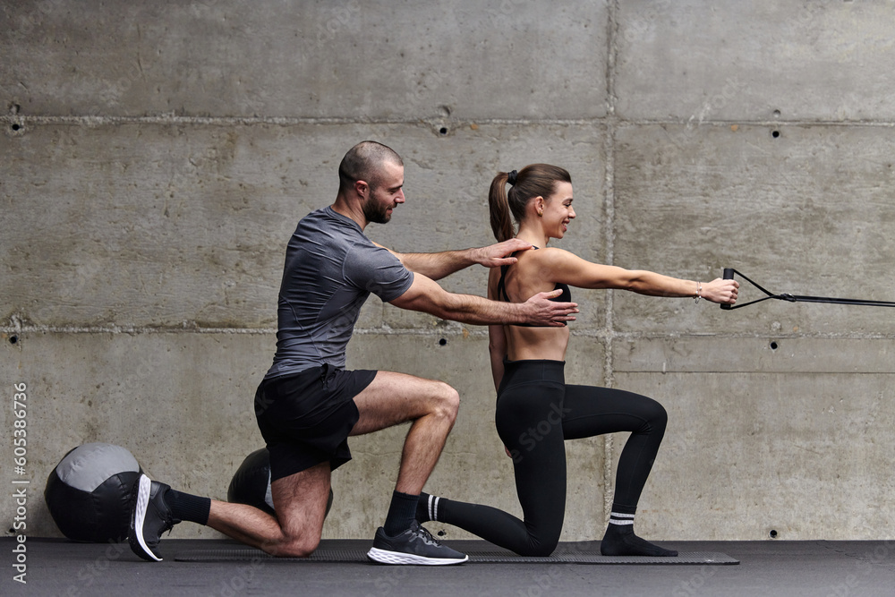 A muscular man assisting a fit woman in a modern gym as they engage in ...