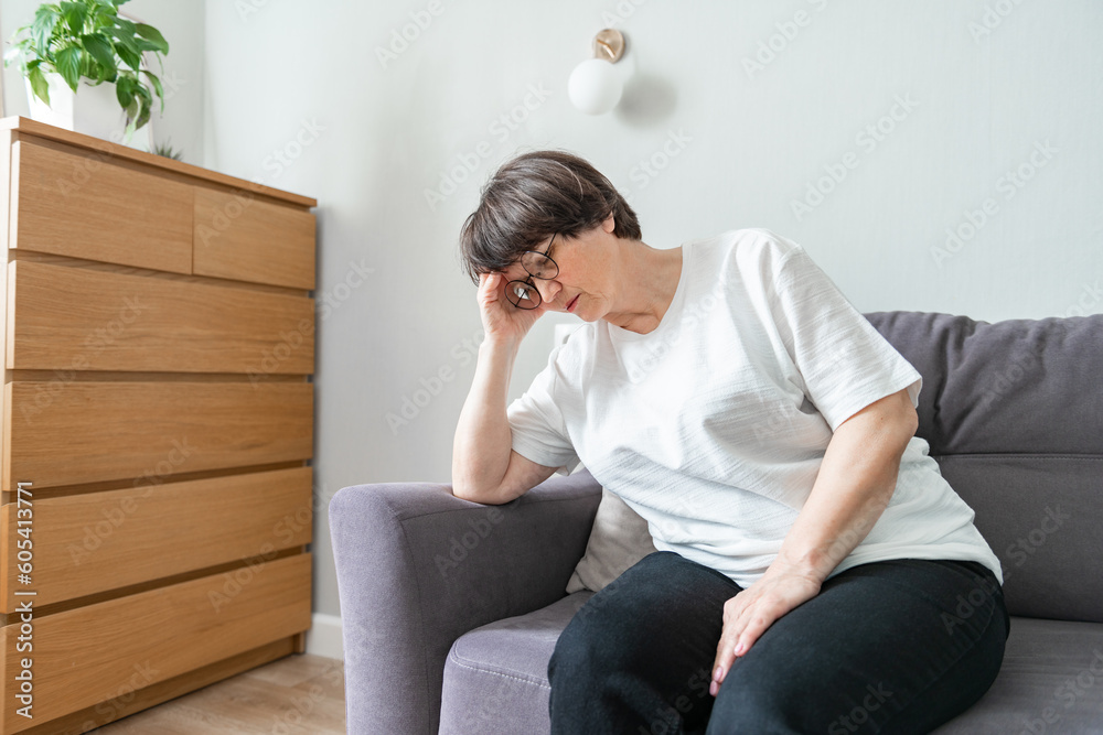 Tired, depressed senior woman sitting on couch in living room feeling ...