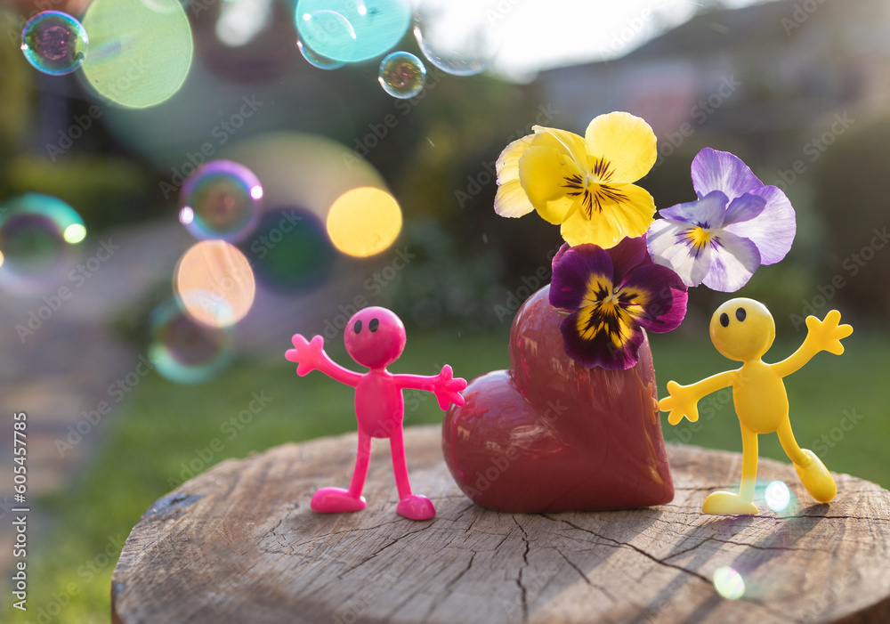 Miniature bright toy figurines of people near heart-shaped vase with ...