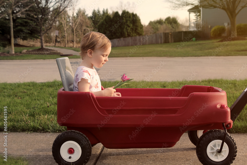 Beautiful young girl sitting in a red wagon cart by the road outdoors ...