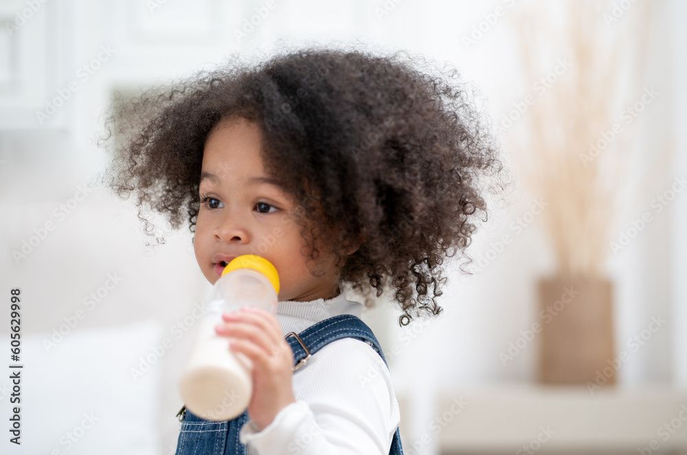 Cute curly hair biracial little girl sucking milk from bottle. Hungry ...