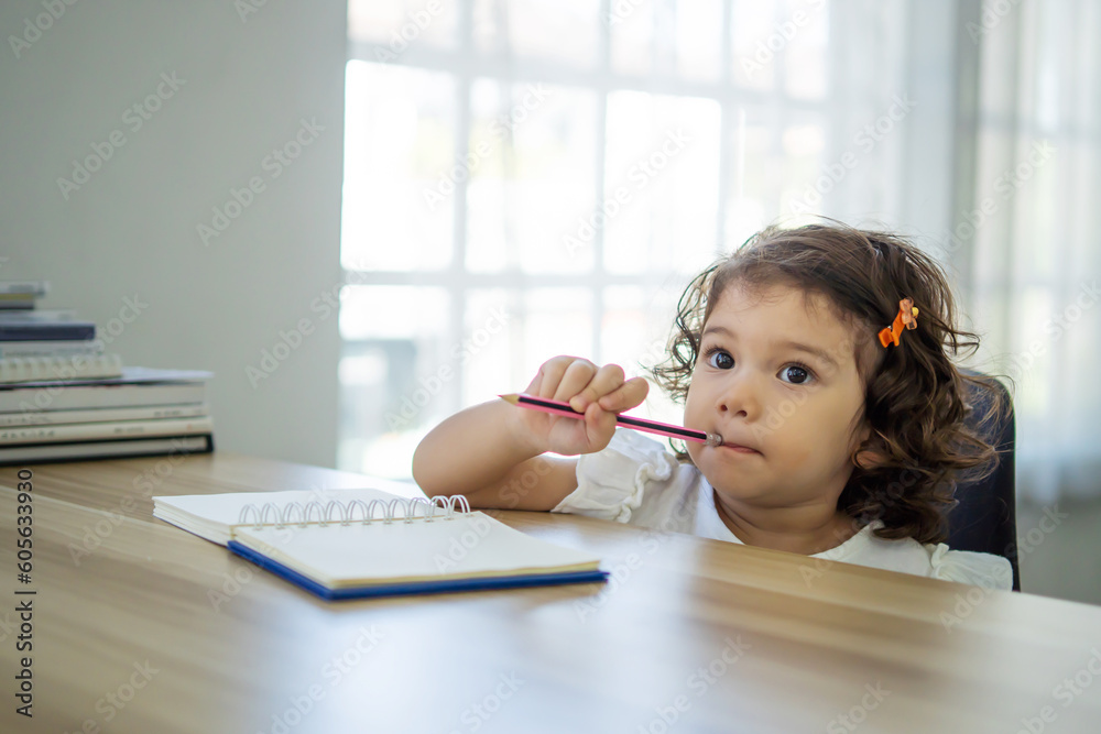 Cute little girl sit at desk at home doing homework, reading, writing ...