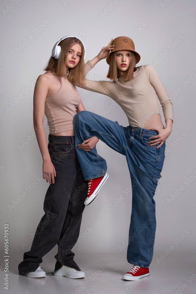 beautiful two girls with a beautiful figure in jeans, a hat, headphones ...