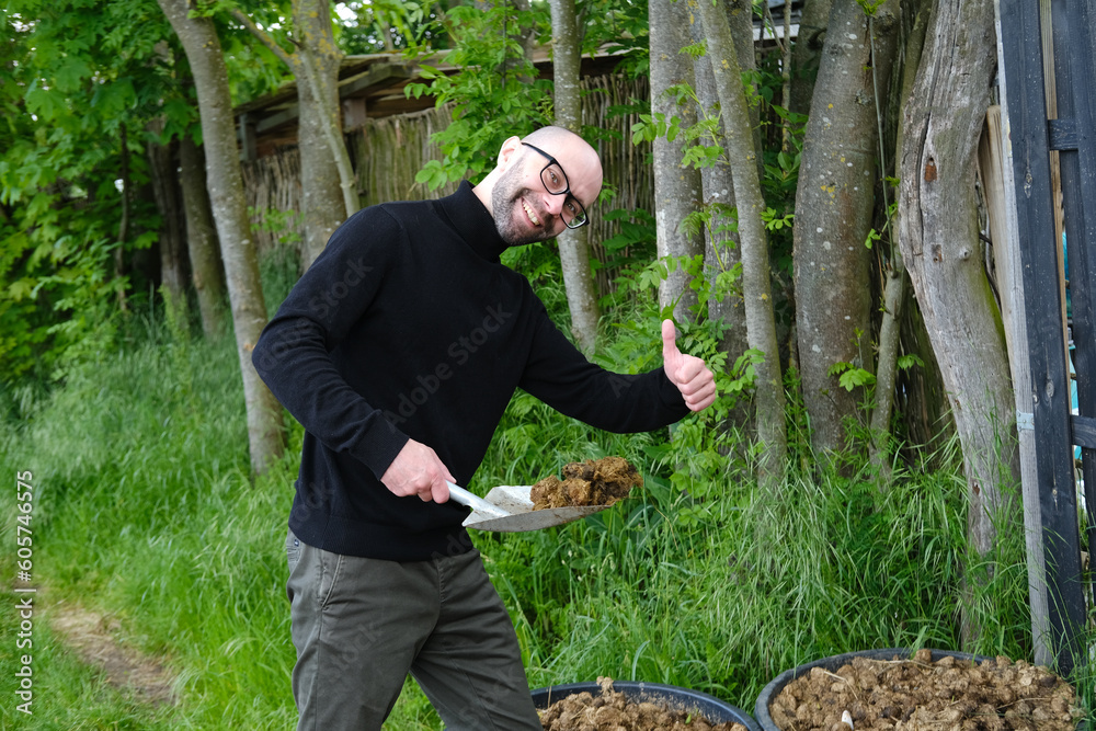 young farmer scoops up horse dung, manure, horse apples, in large ...