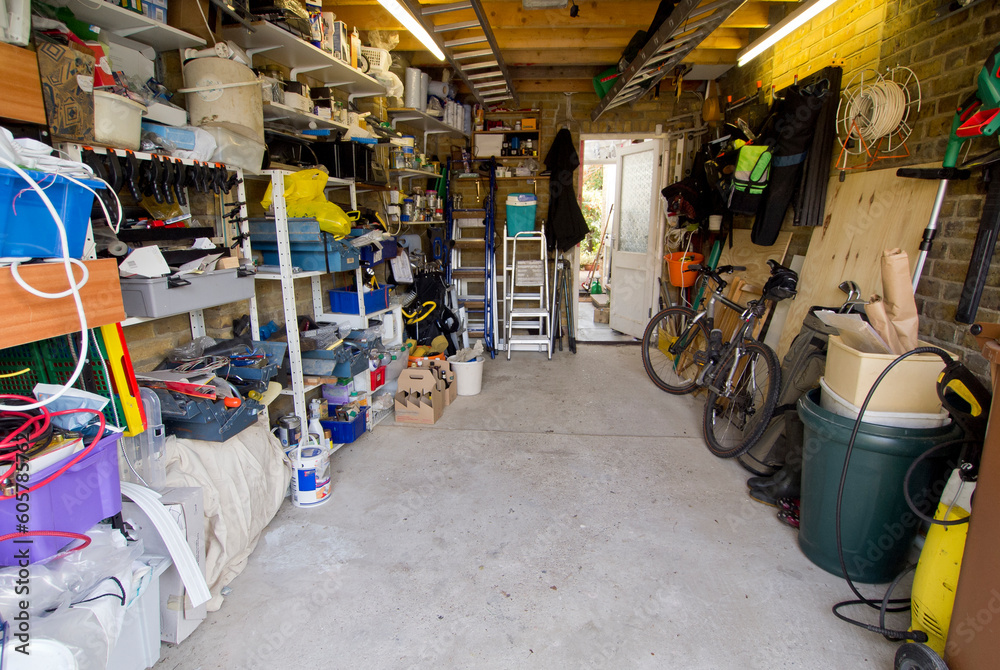 Interior of typical UK garage full of shelves, tools, bikes, paint and ...