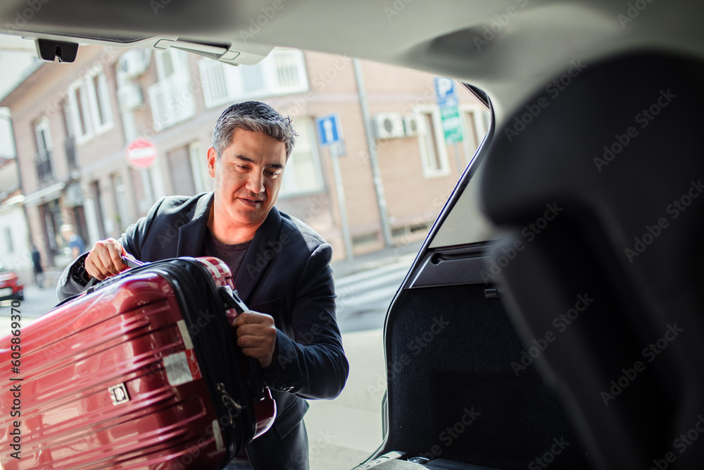 Middle aged man putting a suitcase in the trunk of a car Stock Photo ...