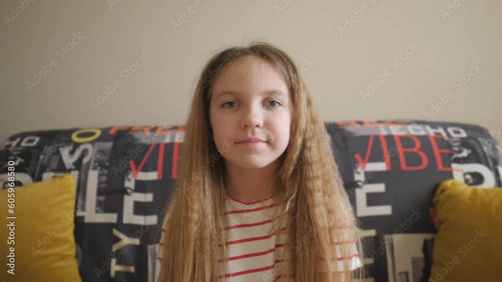 Small disappointed kid sitting on the couch and looking into camera ...