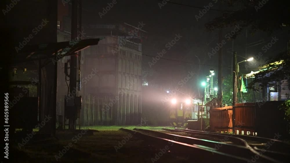 A yellow diesel train pulls into the station at night with lights on ...