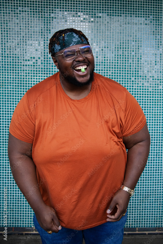 Plus-sized man posing in front of blue tiled wall with bubble gum in ...